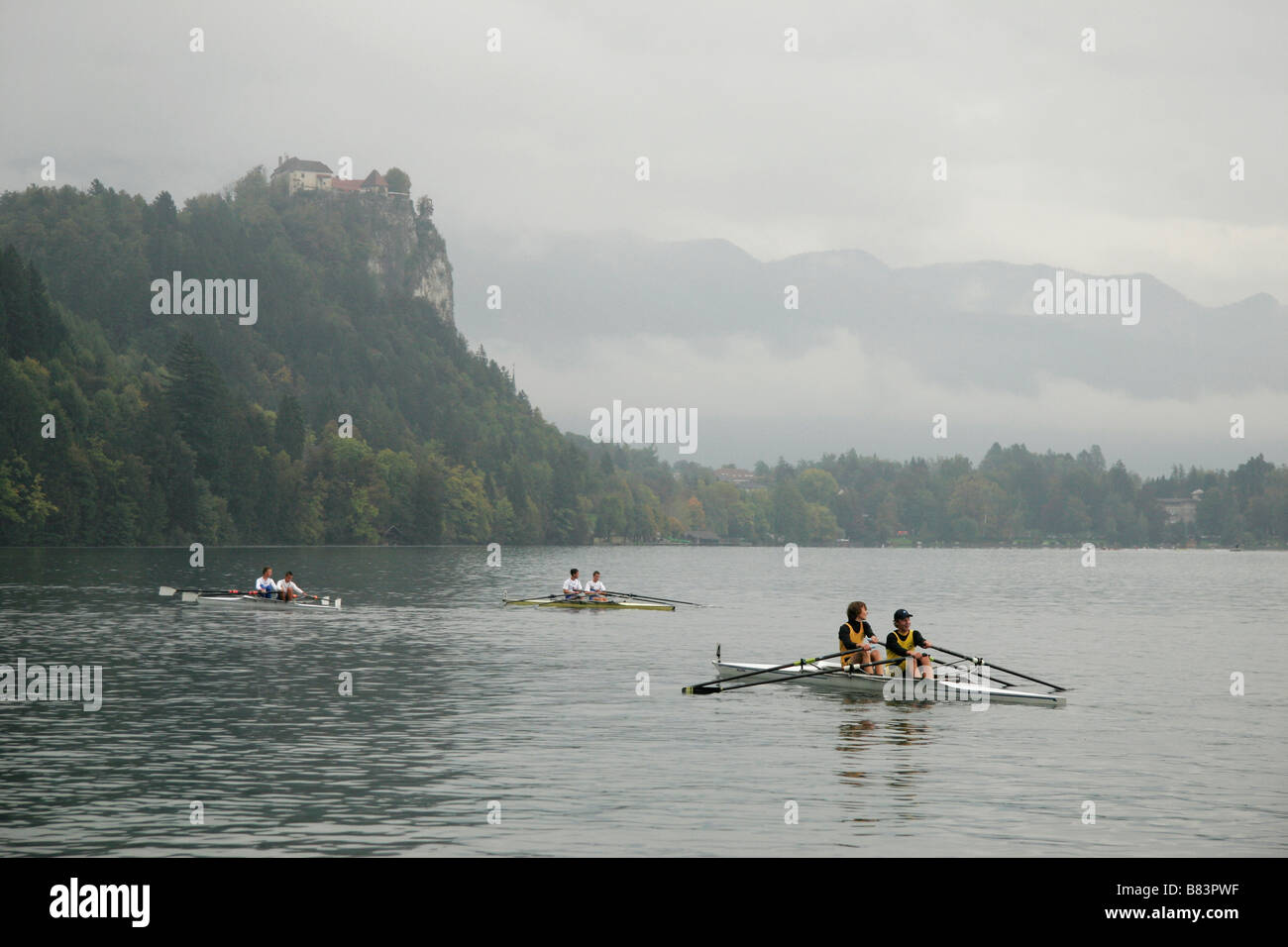 Coxless pairs at a regatta on Lake Bled with Bled Castle perched on the ...