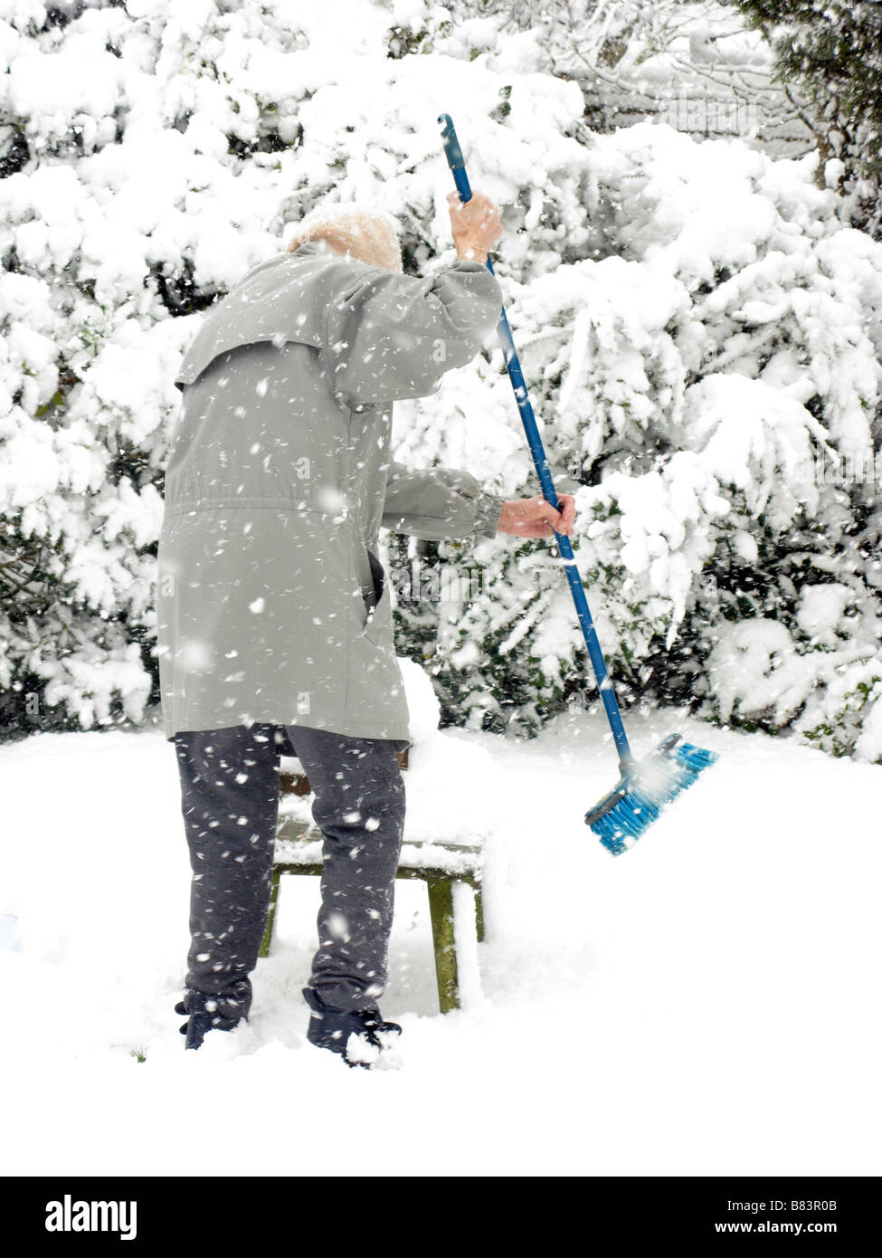 elderly woman wrapped up warmly sweeping snow in snowy conditions Stock ...