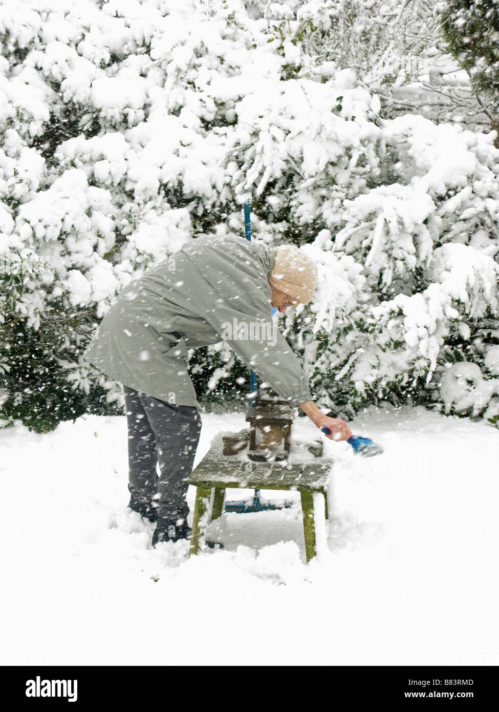 elderly woman wrapped up warmly sweeping snow in snowy conditions Stock ...