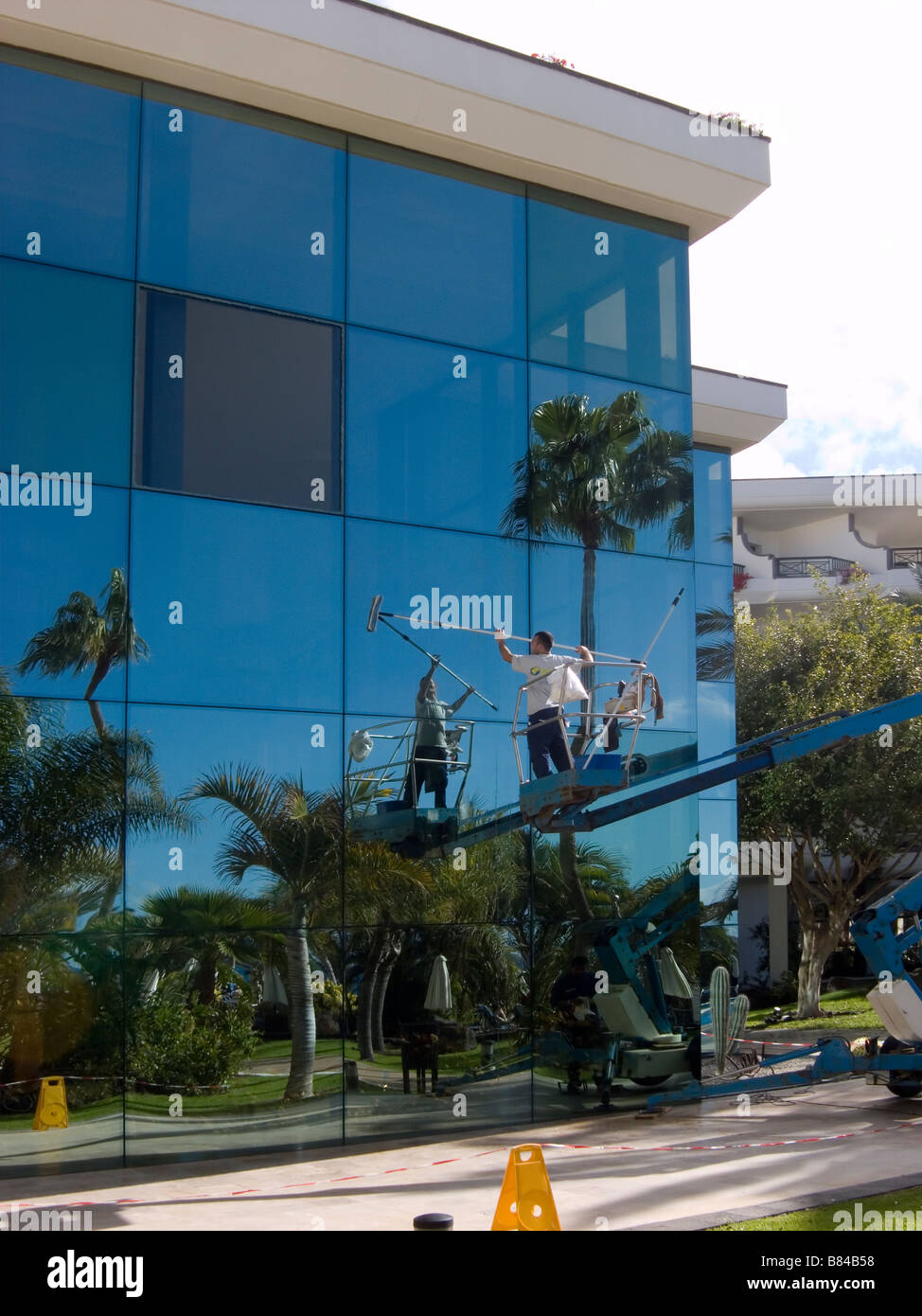 Window cleaner on a hydraulic platform cleaning a large reflective ...