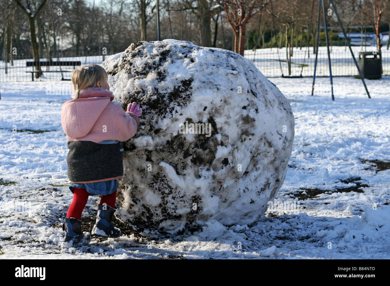 Little girl (3 years old) attempting to push a giant snowball Stock ...
