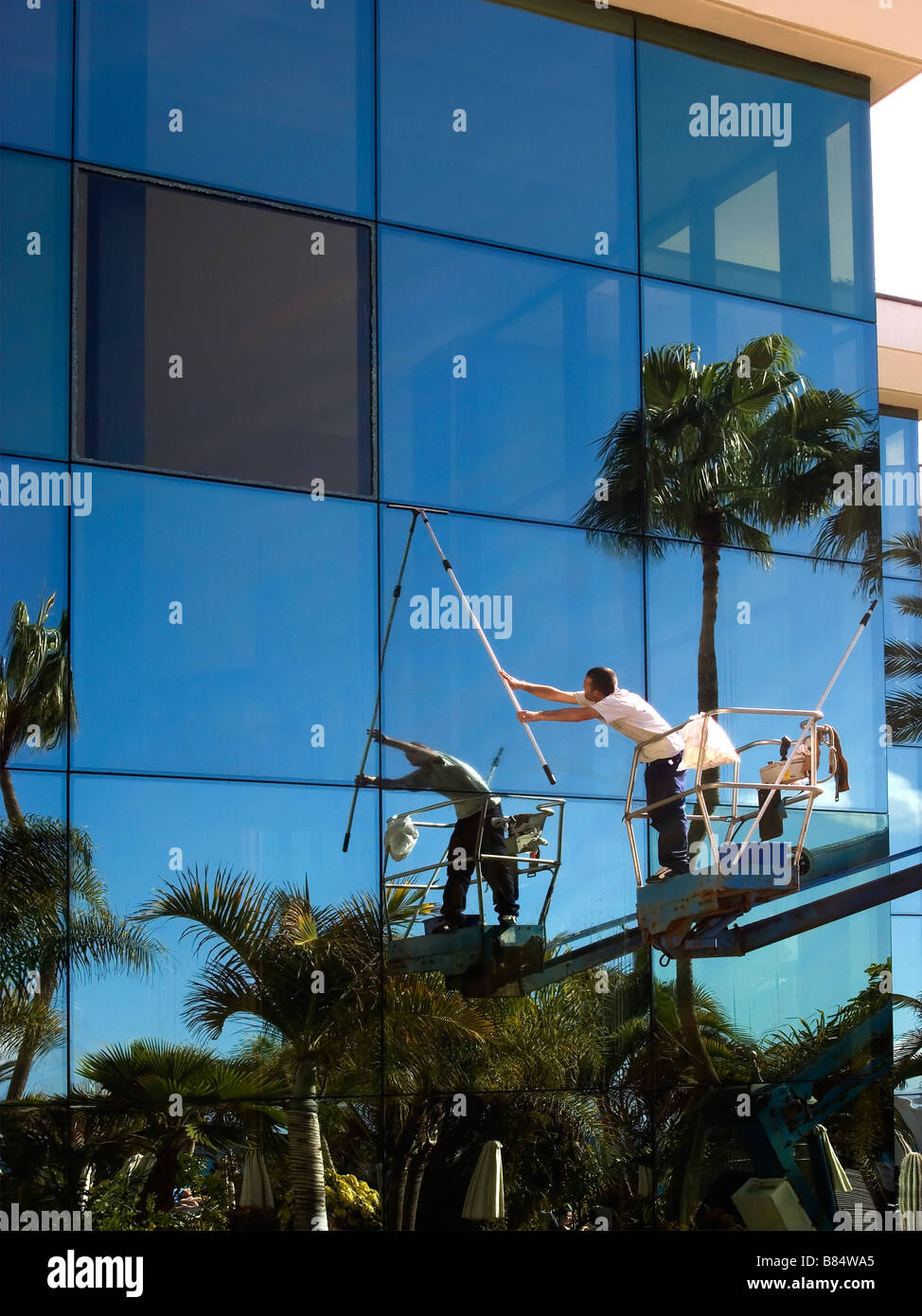 Window cleaner on a hydraulic platform cleaning a large reflective ...