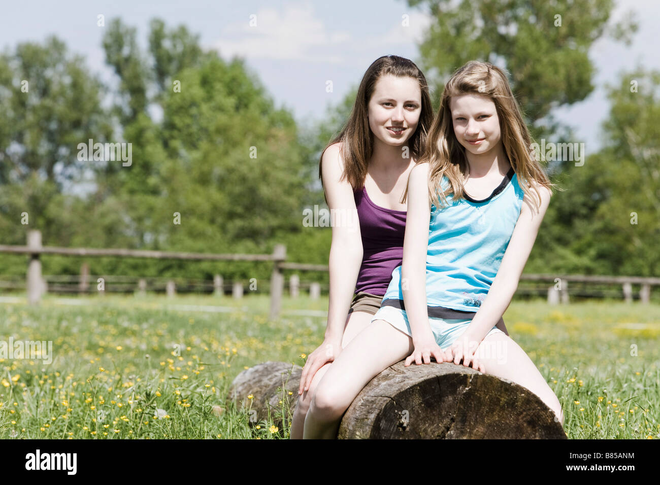 portrait of two girls sitting on tree trunk together Stock Photo - Alamy