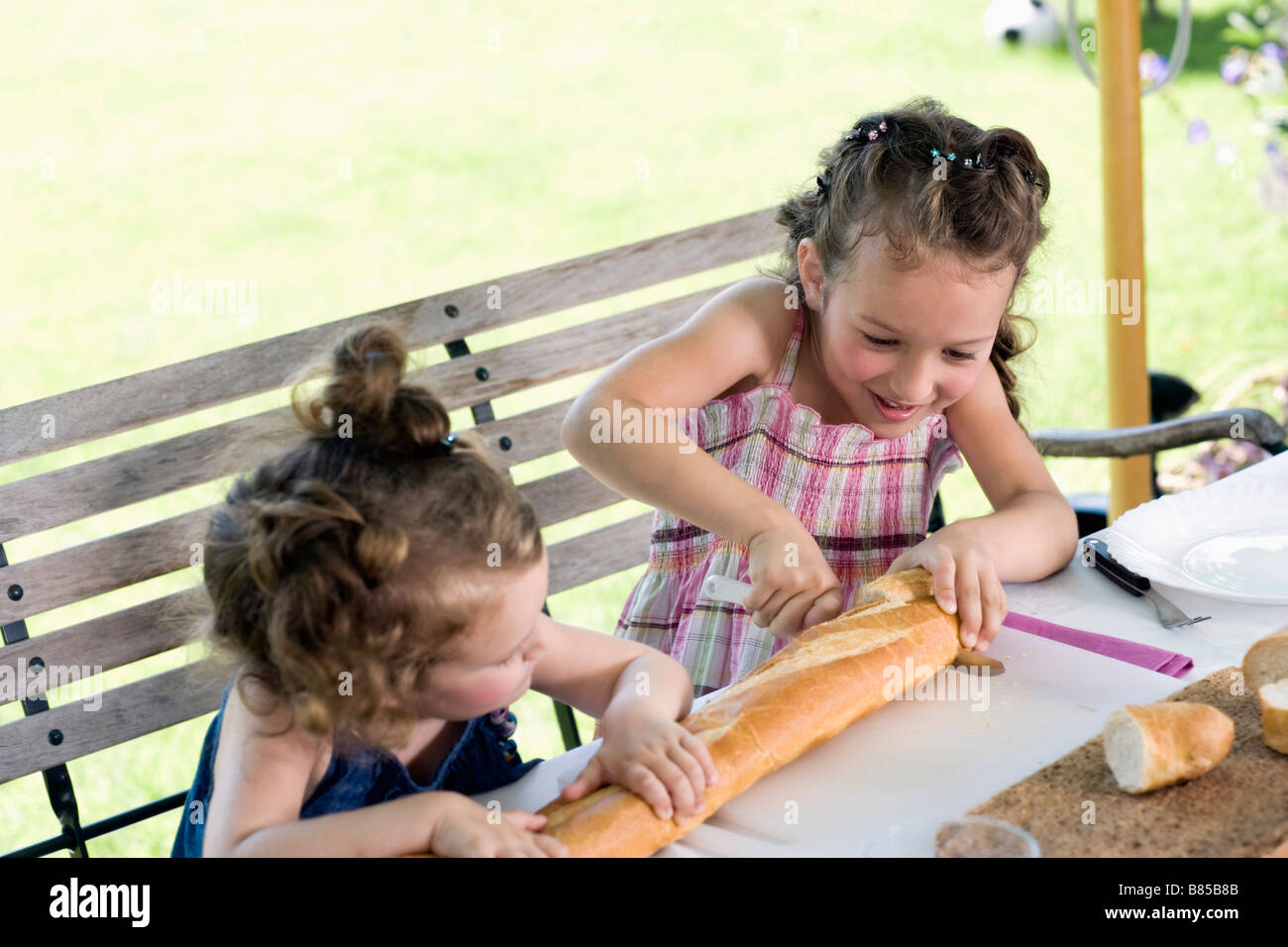 two little sisters sharing bread at table in garden Stock Photo - Alamy