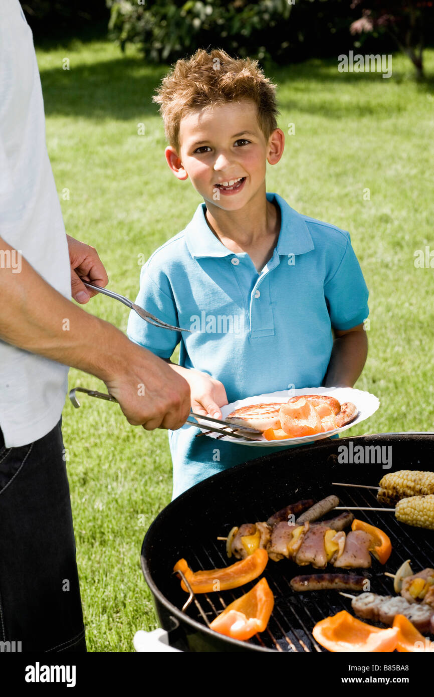 father and son grilling together at barbecue boy holding plate with ...