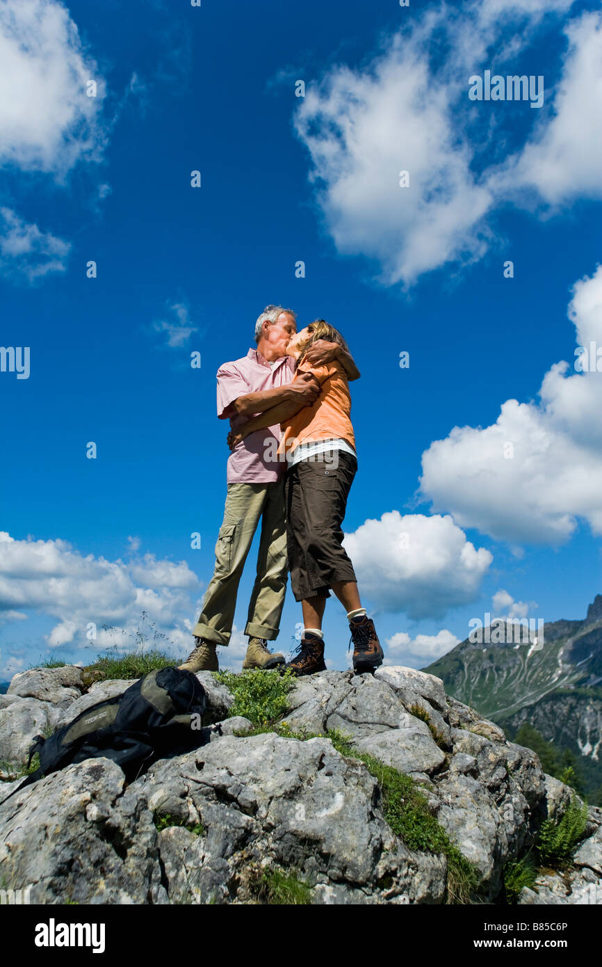 mature couple standing on rock in the mountains kissing each other ...