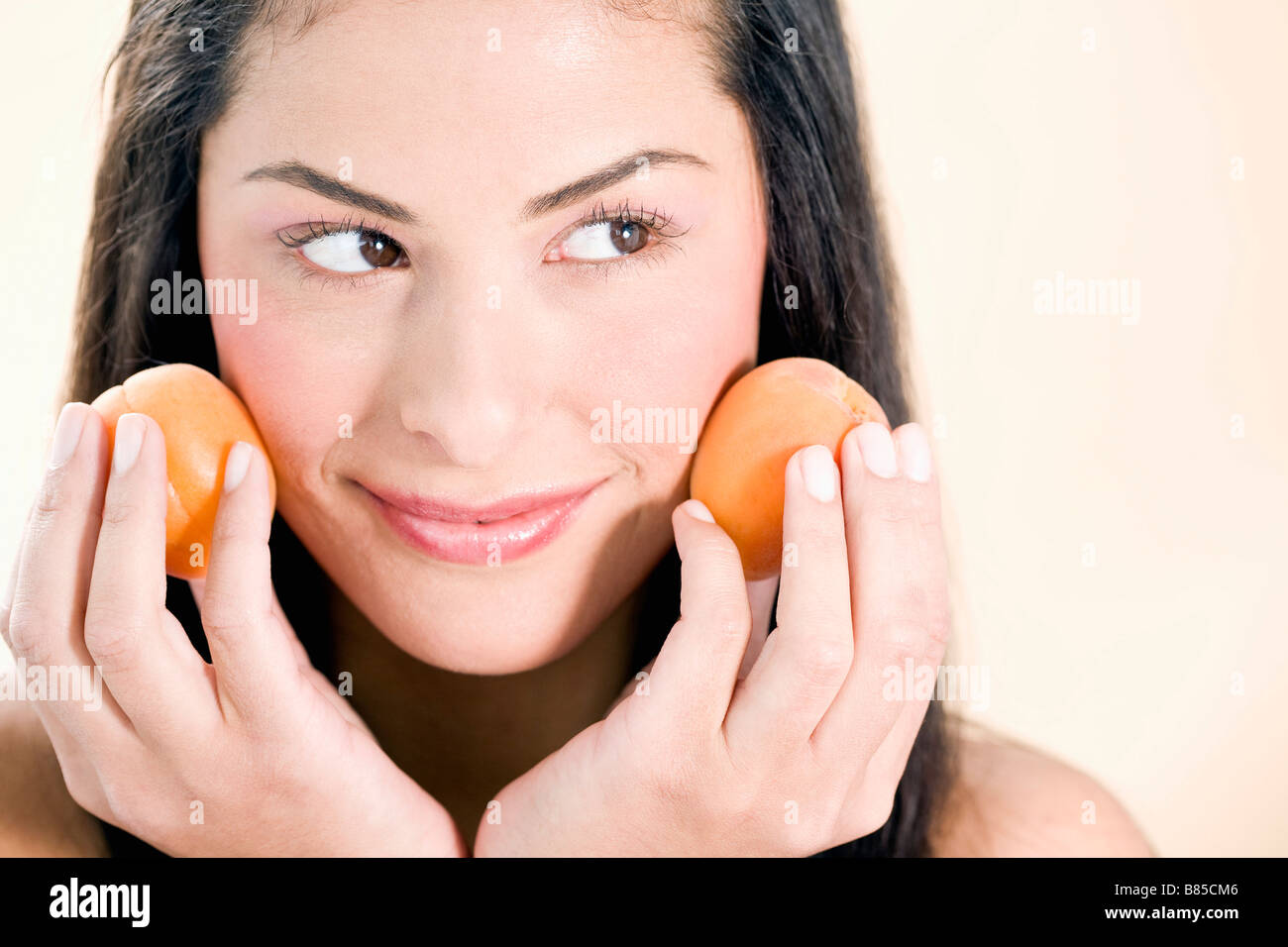 headshot of young woman holding peaches against her cheek Stock Photo ...