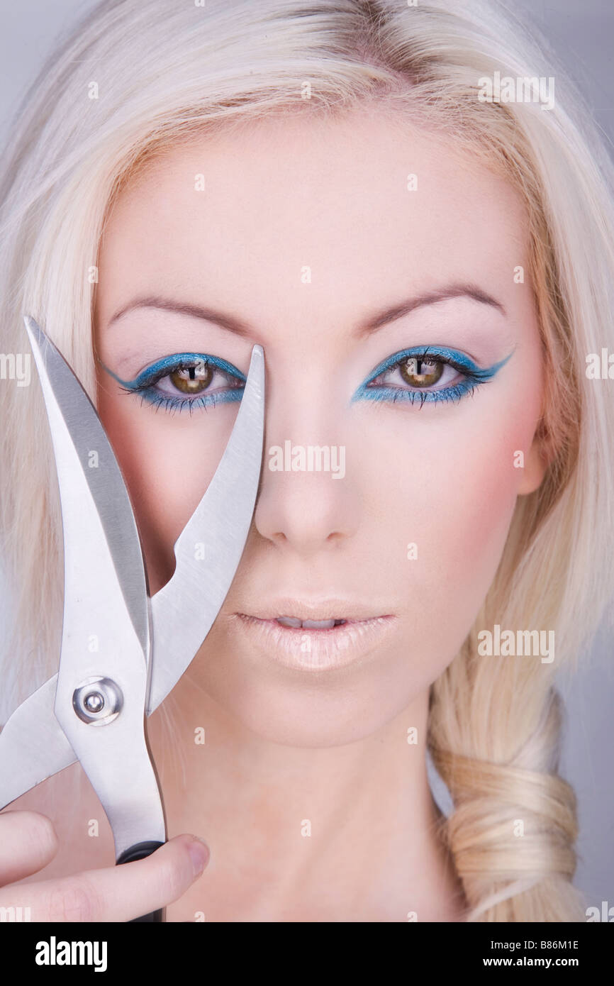 young pretty girl with clear skin holding scissors towards her face ...