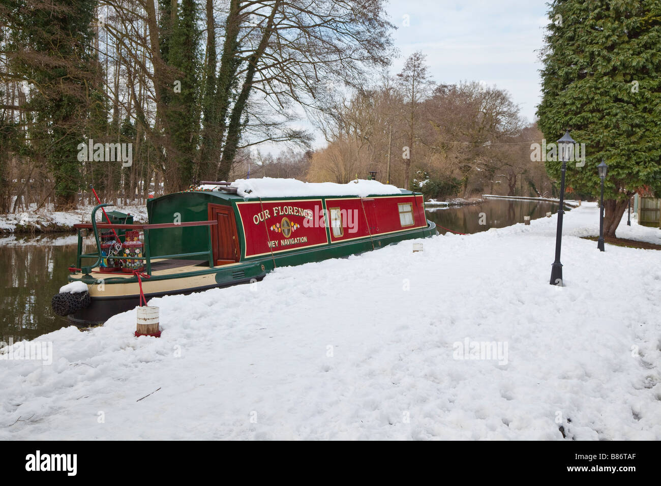 A canal barge in the snow tied up to posts on the bank of the river Wey ...