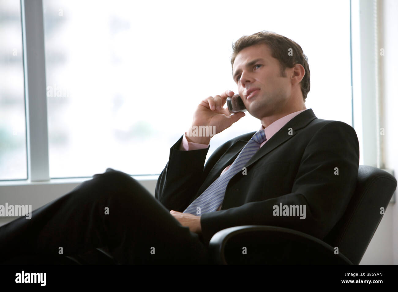 Businessman sitting on armchair using cell phone Stock Photo - Alamy
