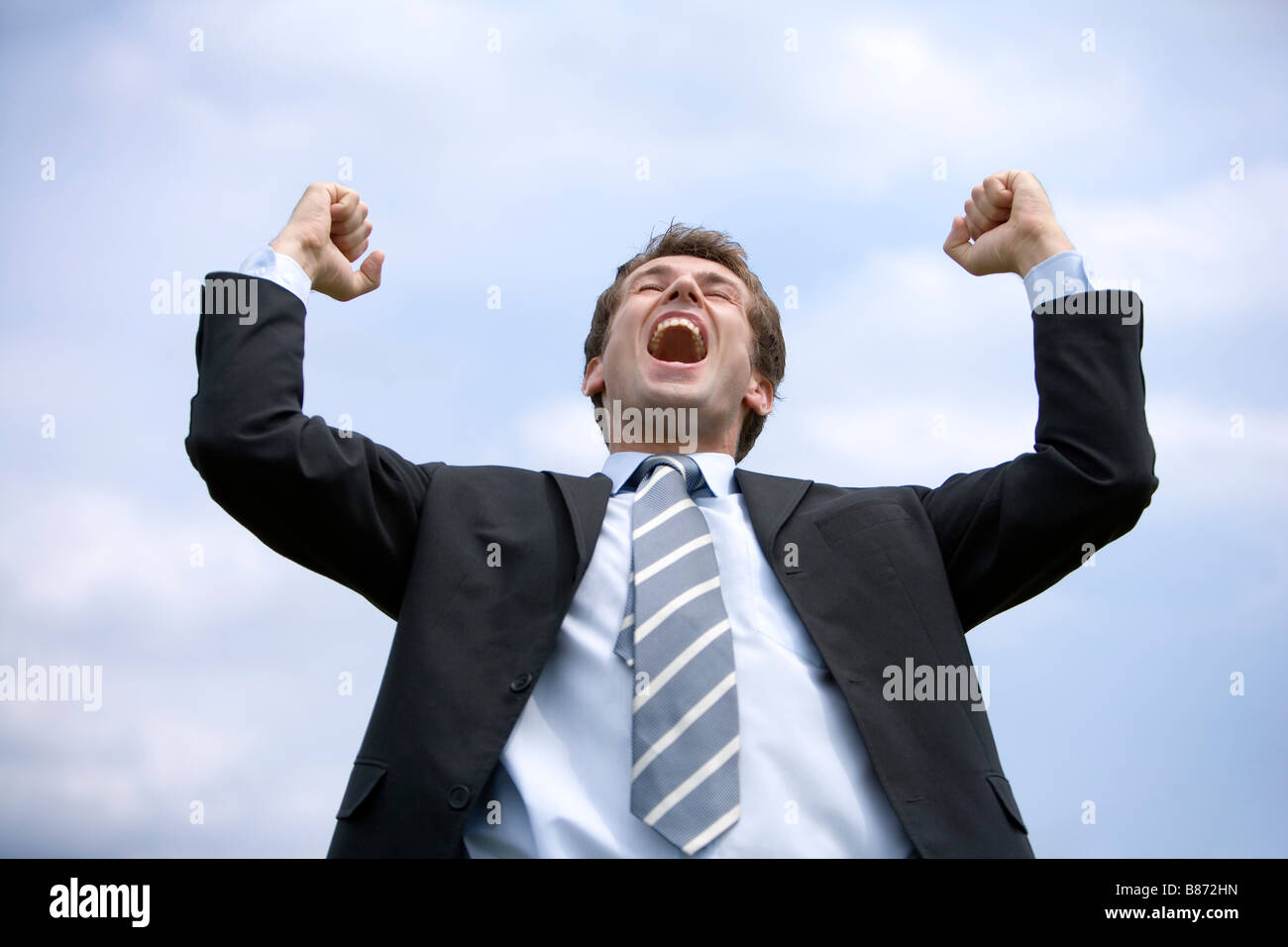 Businessman raising arms clenching fists smiling view from below Stock ...