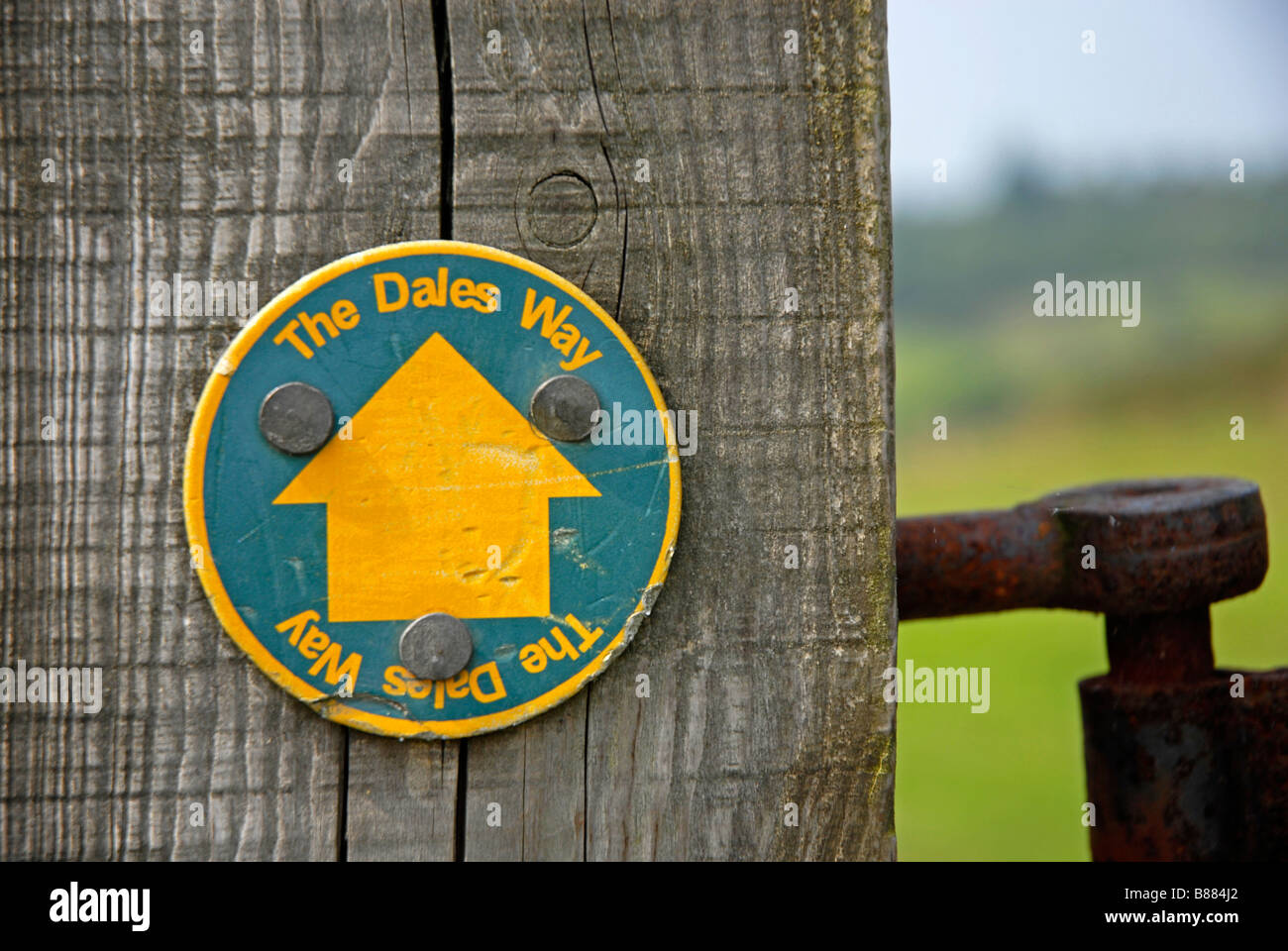 Round sign, nailed to wooden gate post, with broad yellow arrow ...