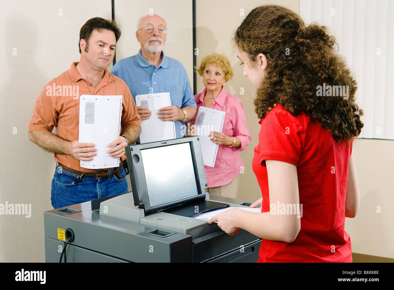 Young woman voting on optical scan machine as a line of people waits ...