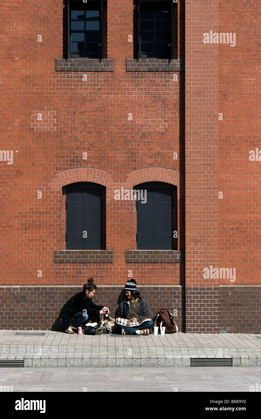 A young couple and their dog sit in the sun at the Aka renga soko red ...