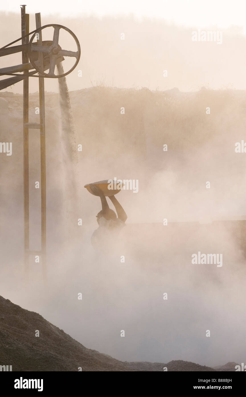 Indian men putting crushed stone into a trailer, surrounded by dust ...