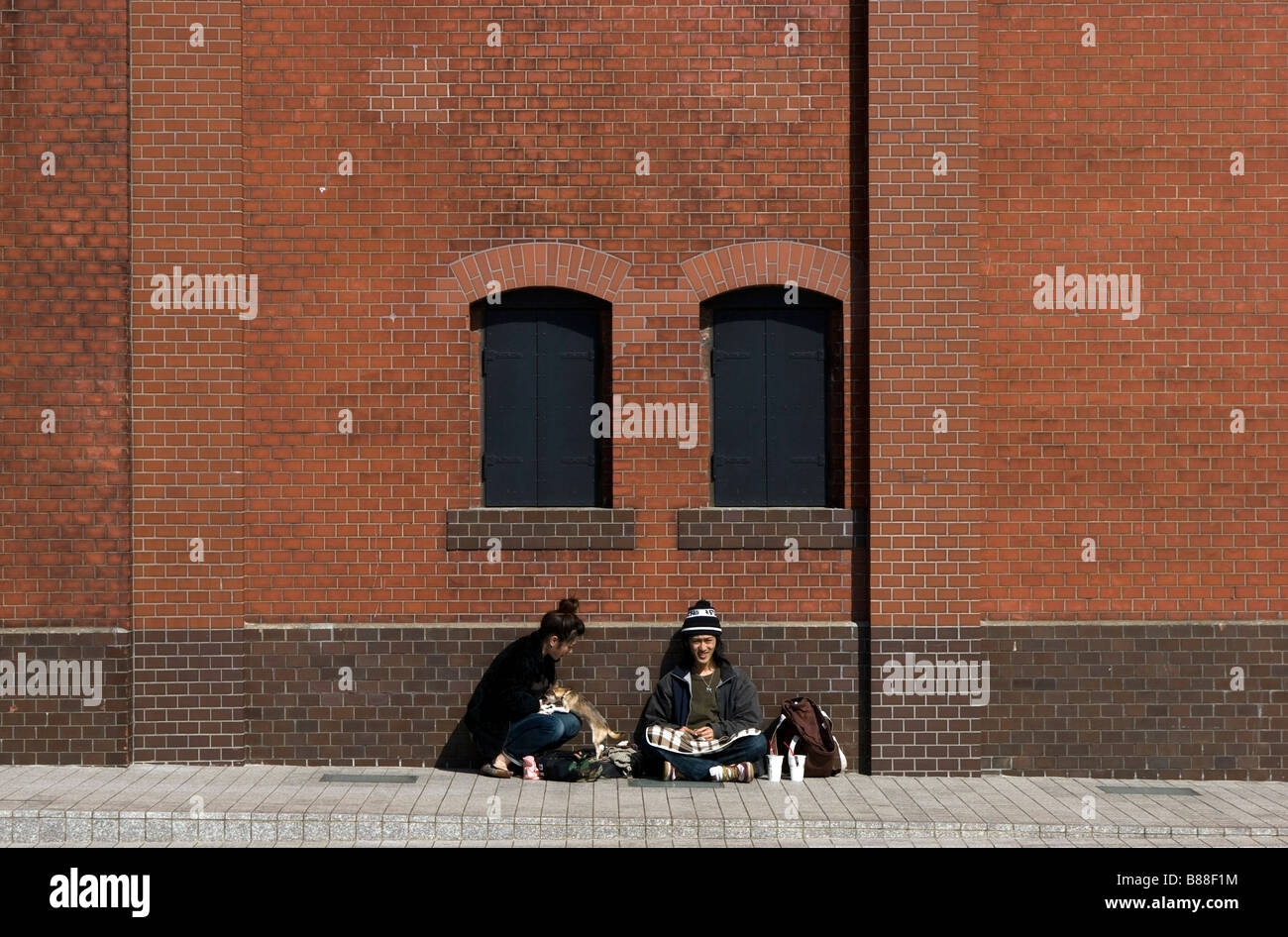 A young couple and their dog sit in the sun at the Aka renga soko red ...