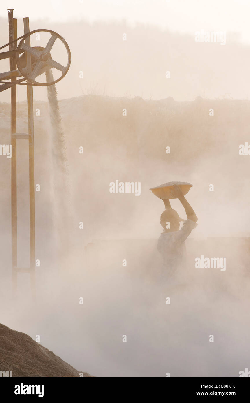 Indian men putting crushed stone into a trailer, surrounded by dust ...