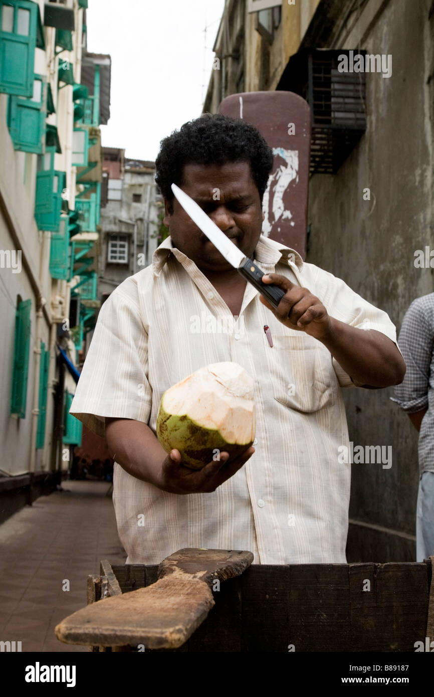 Coconut seller opens a coconut which he has just sold, in Mumbai. India ...