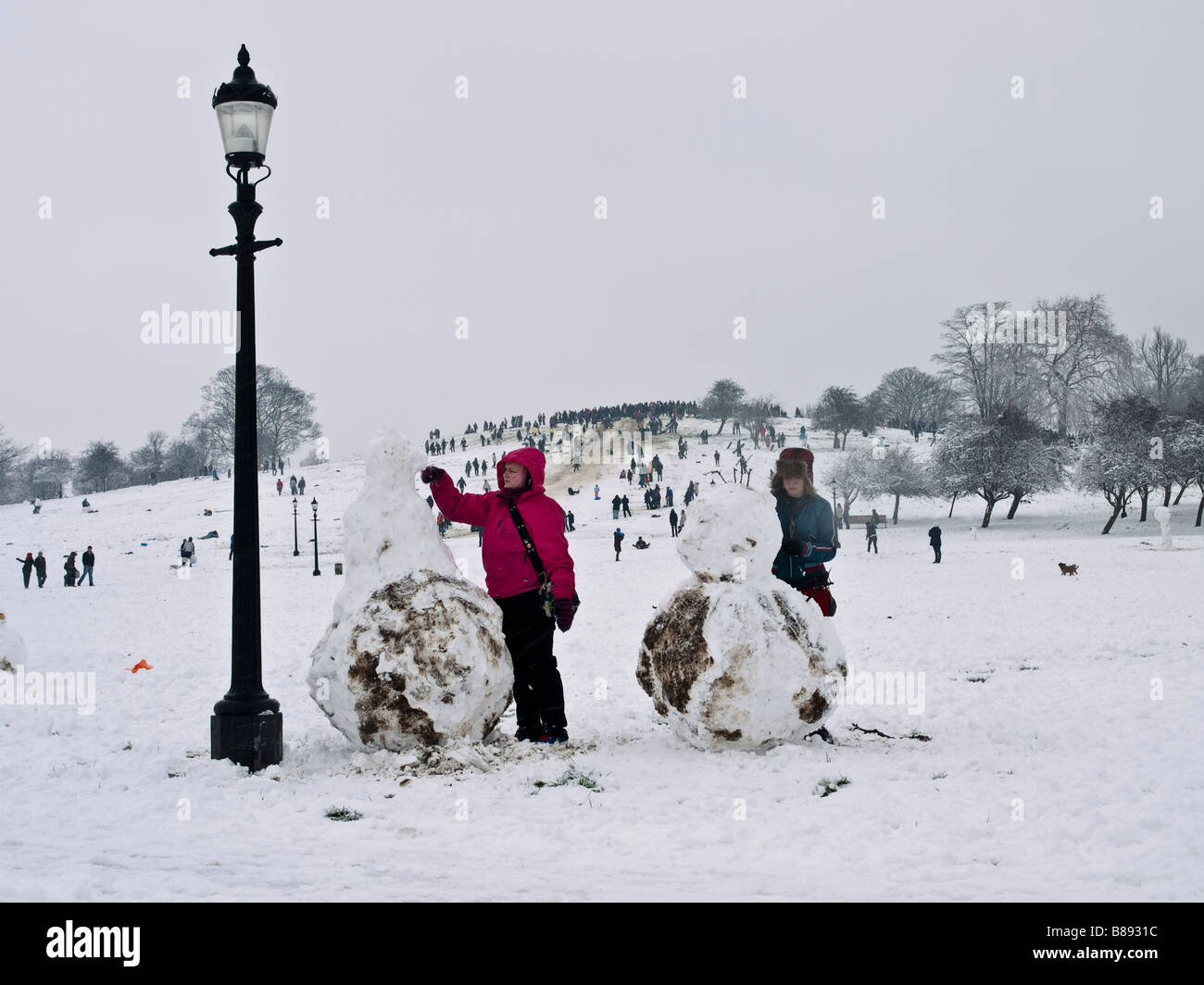 2 people building big snowmen next to an old-fashioned lamp on Primrose ...