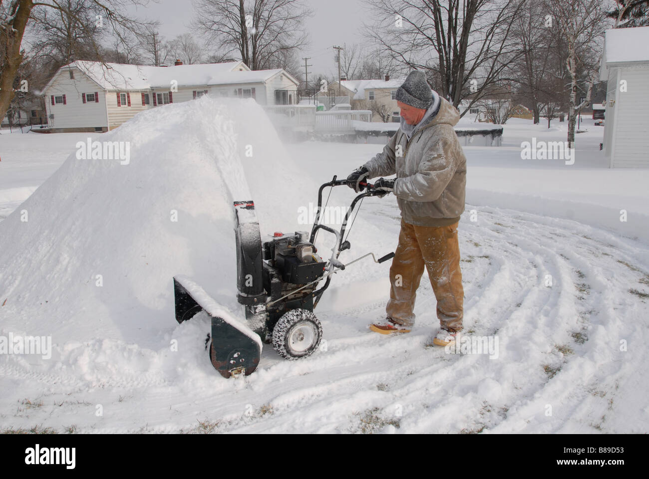 A man dressed in warm clothes operates a snowblower to move snow in the ...