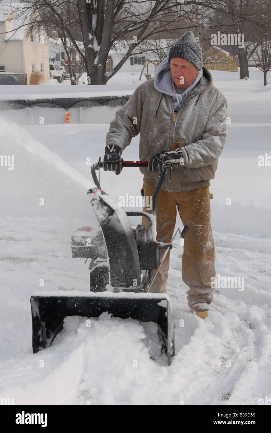 A man dressed in warm clothes operates a snowblower to move snow in the ...