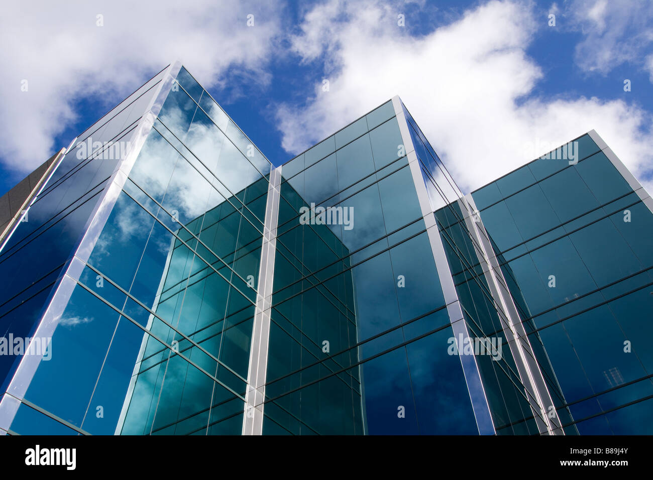Three towers of a sleek modern glass office building with clouds and ...