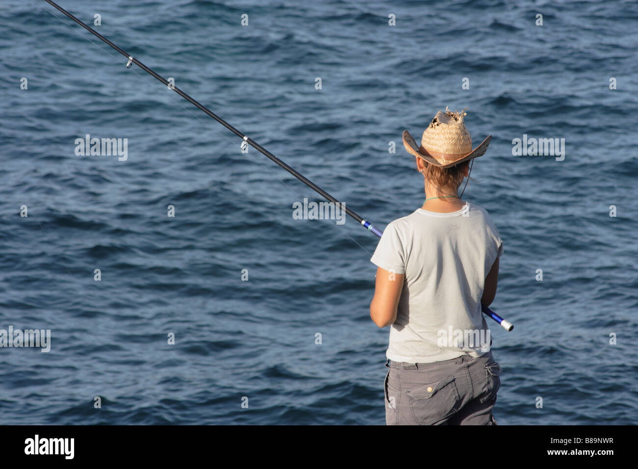 Rear view of woman wearing straw hat fishing from rocks in Spain Stock ...