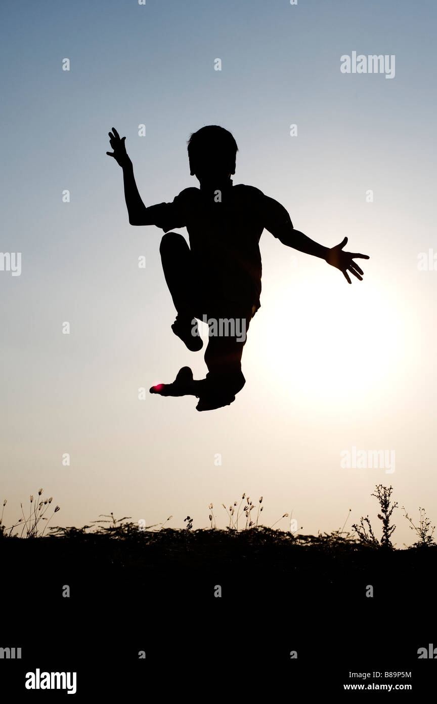 Silhouette profile of a young Indian boy jumping against a setting sun ...
