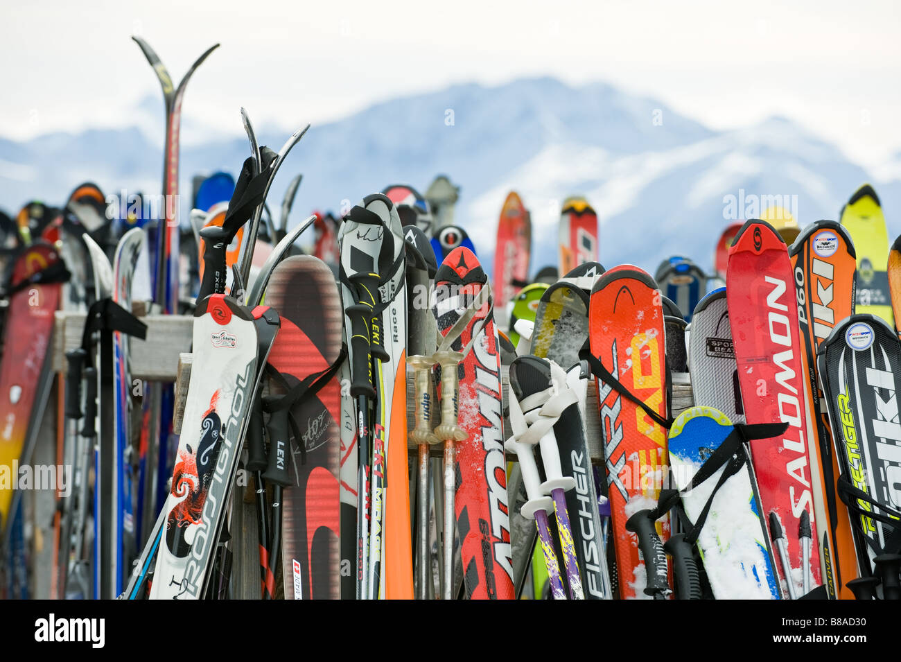 Wide image of a rack of skis and ski poles with snowy mountains in the ...