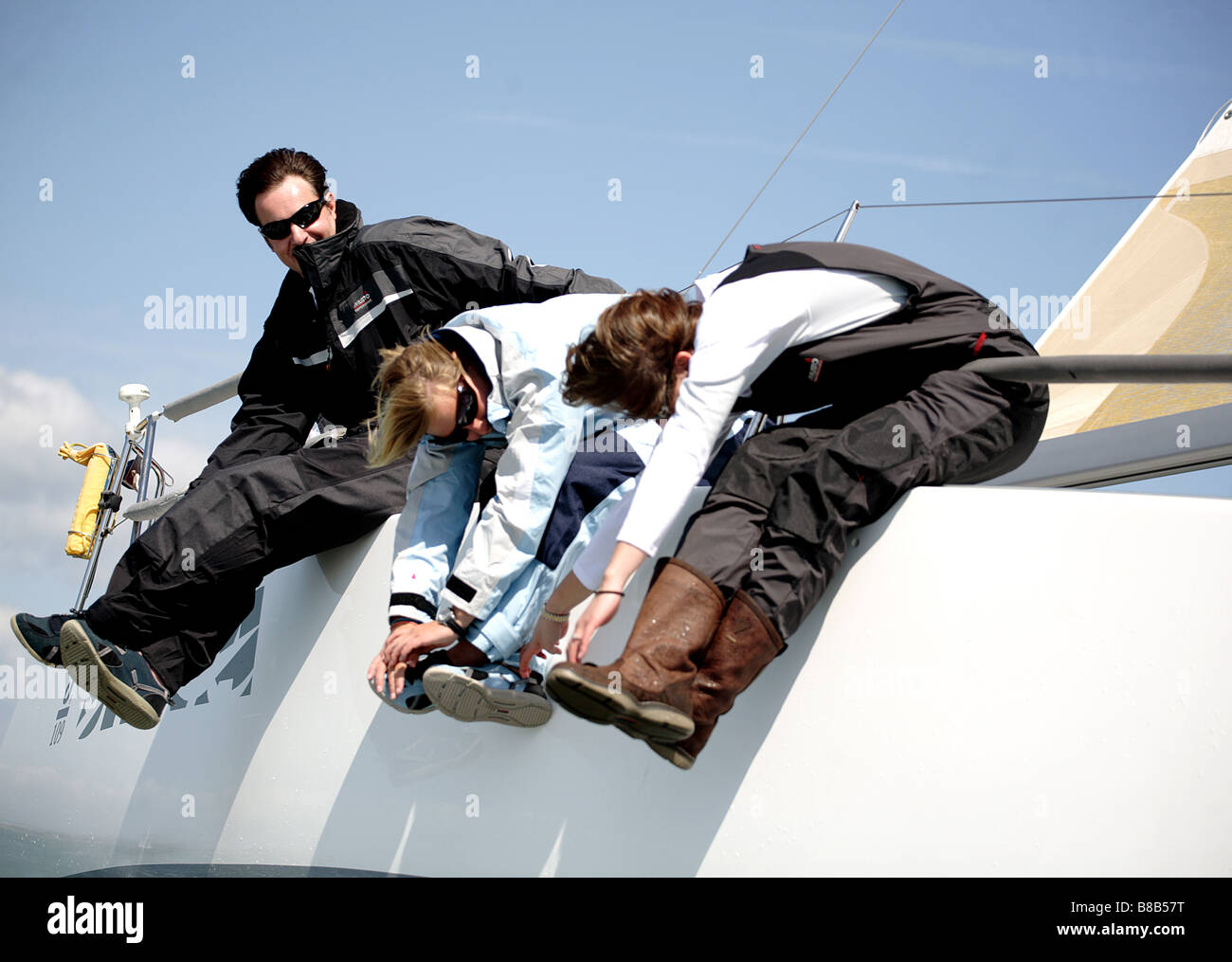 3 sailors 2 female 1 male having fun on the side of a yacht. The ...