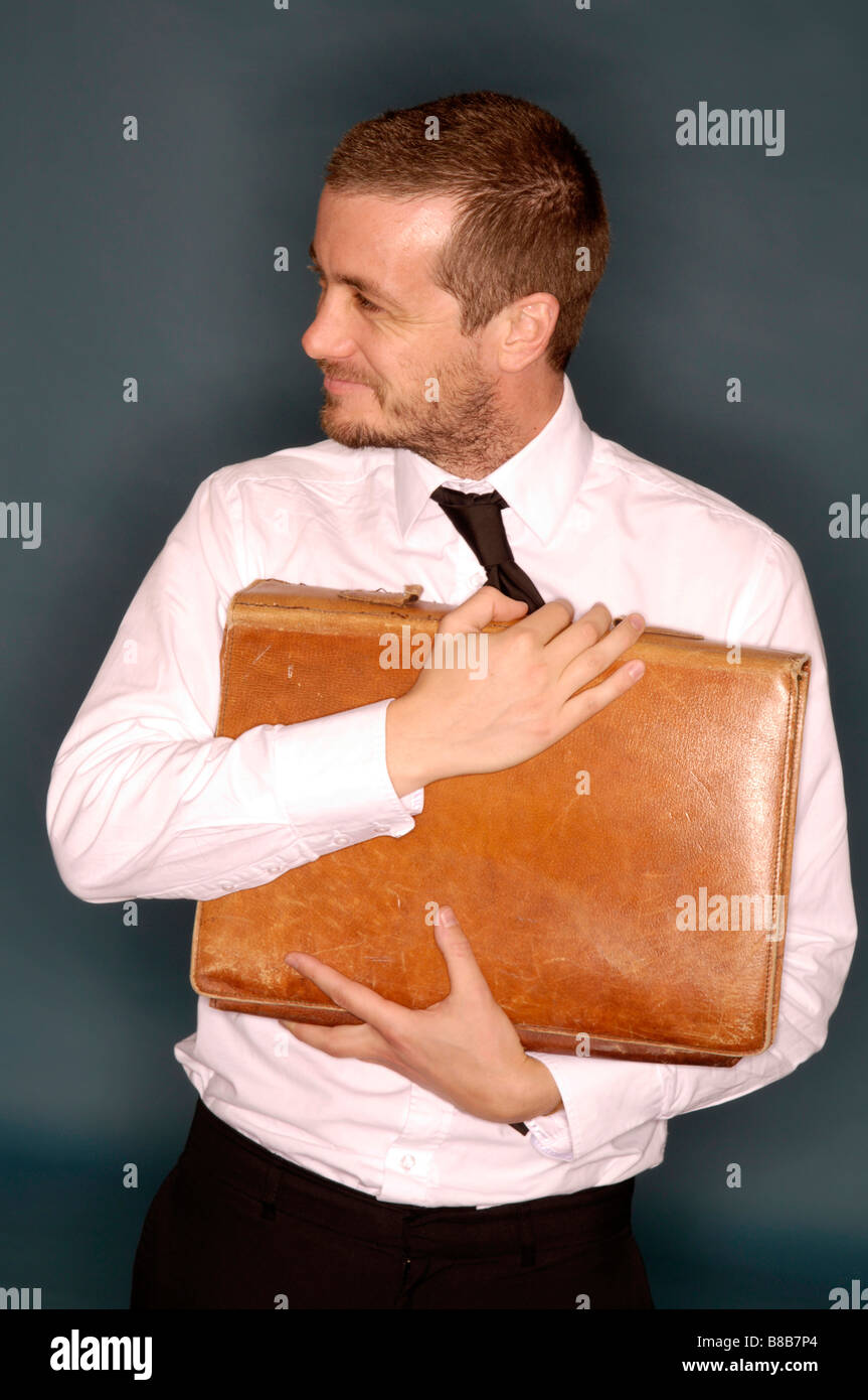 a businessman stands holding brown leather briefcase in hand smiling ...