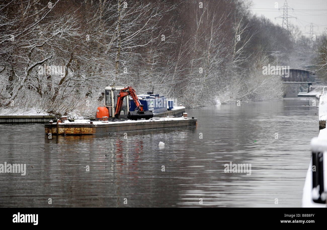 A dredger lifts silt from a canal into a barge during winter snow Stock ...