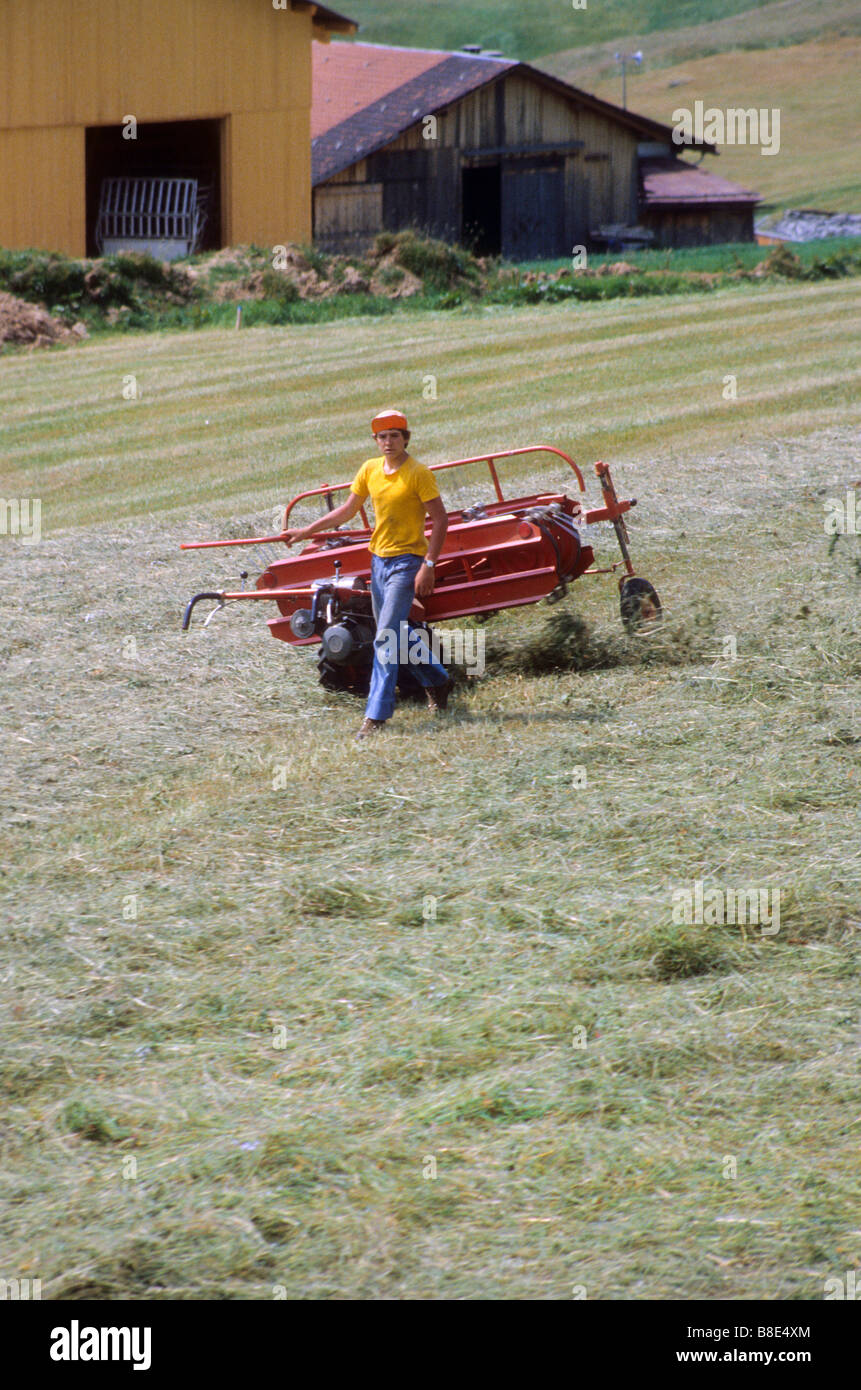 Teen boy operates rake machine that turns the grass on his farm in ...