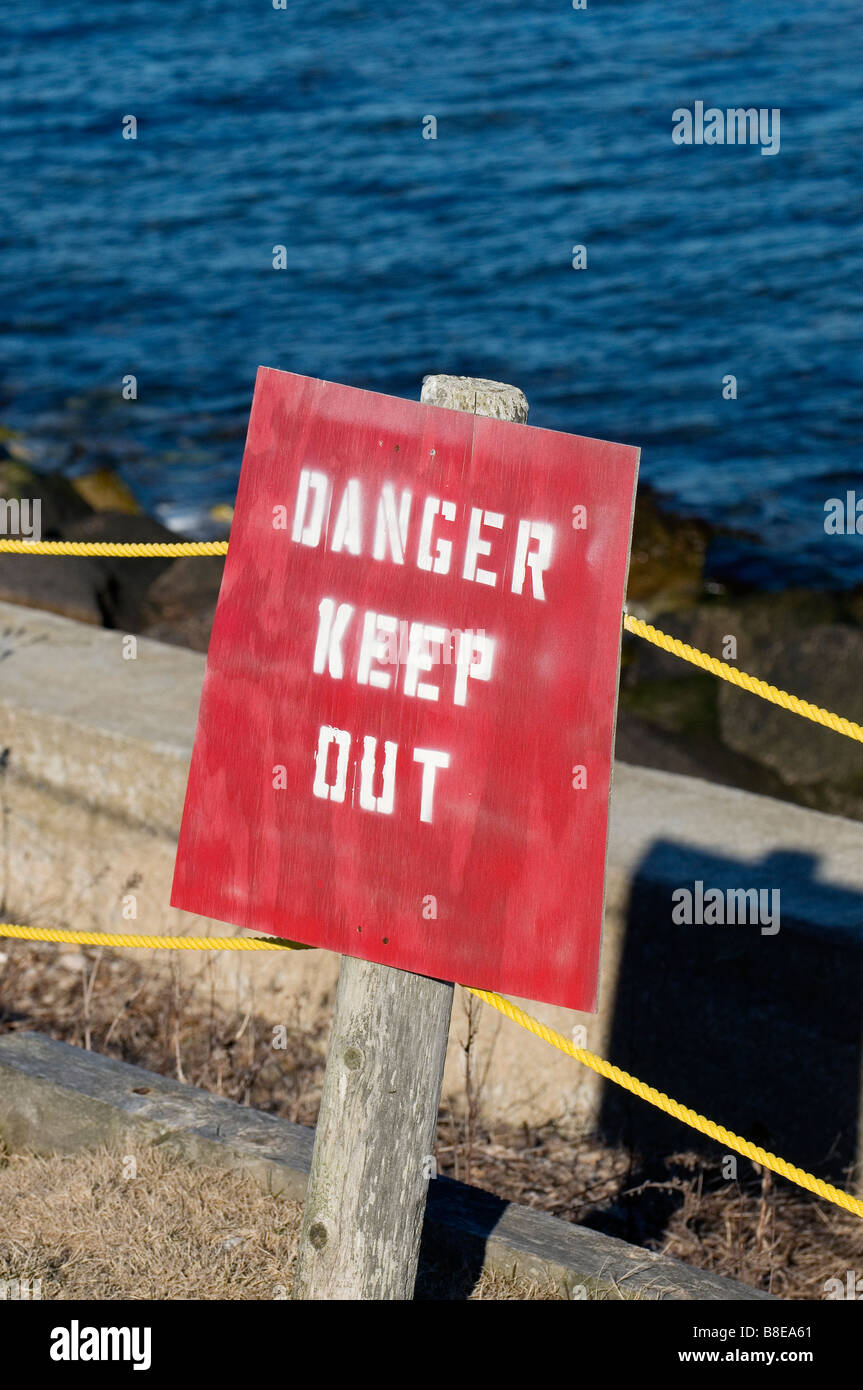 A red danger keep out sign along wall and rocky shore at Point Judith ...