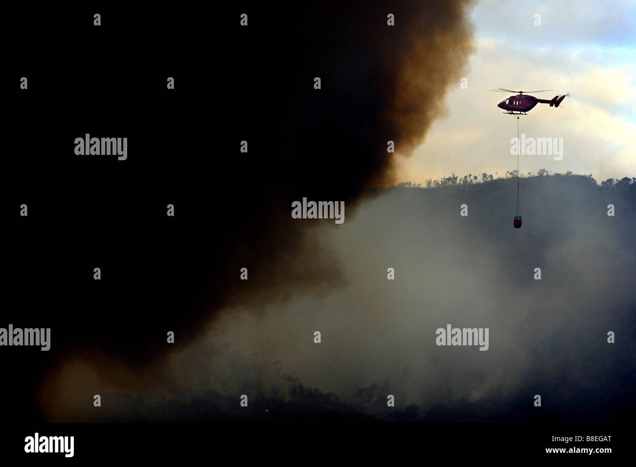 a helicopter with monsoon bucket fighting a bush fire in New Zealand ...