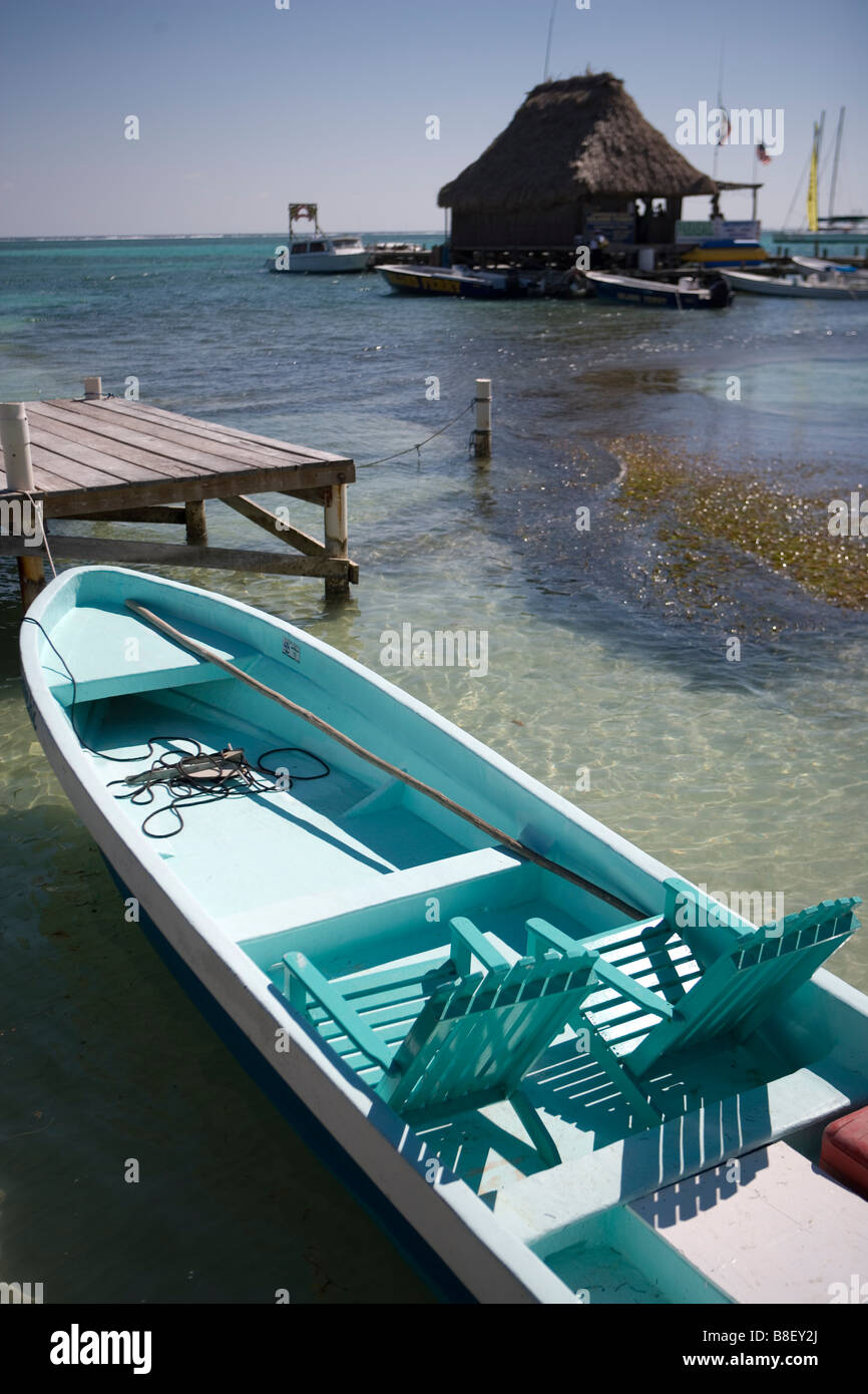 A bright teal boat and chairs sit in the shallows tied to a pier on ...