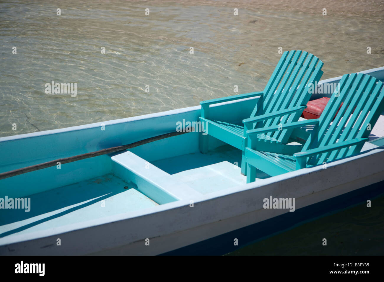 A bright teal boat and chairs sit in the shallows tied to a pier on ...