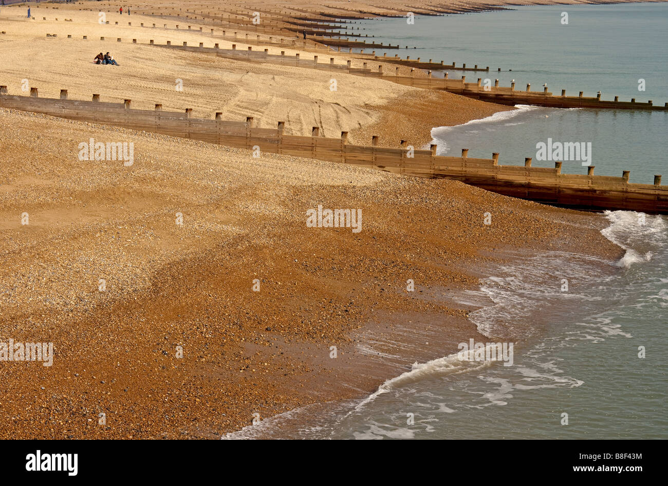 Tourists sits on beach on Eastbourne seafront in the sun with a calm ...