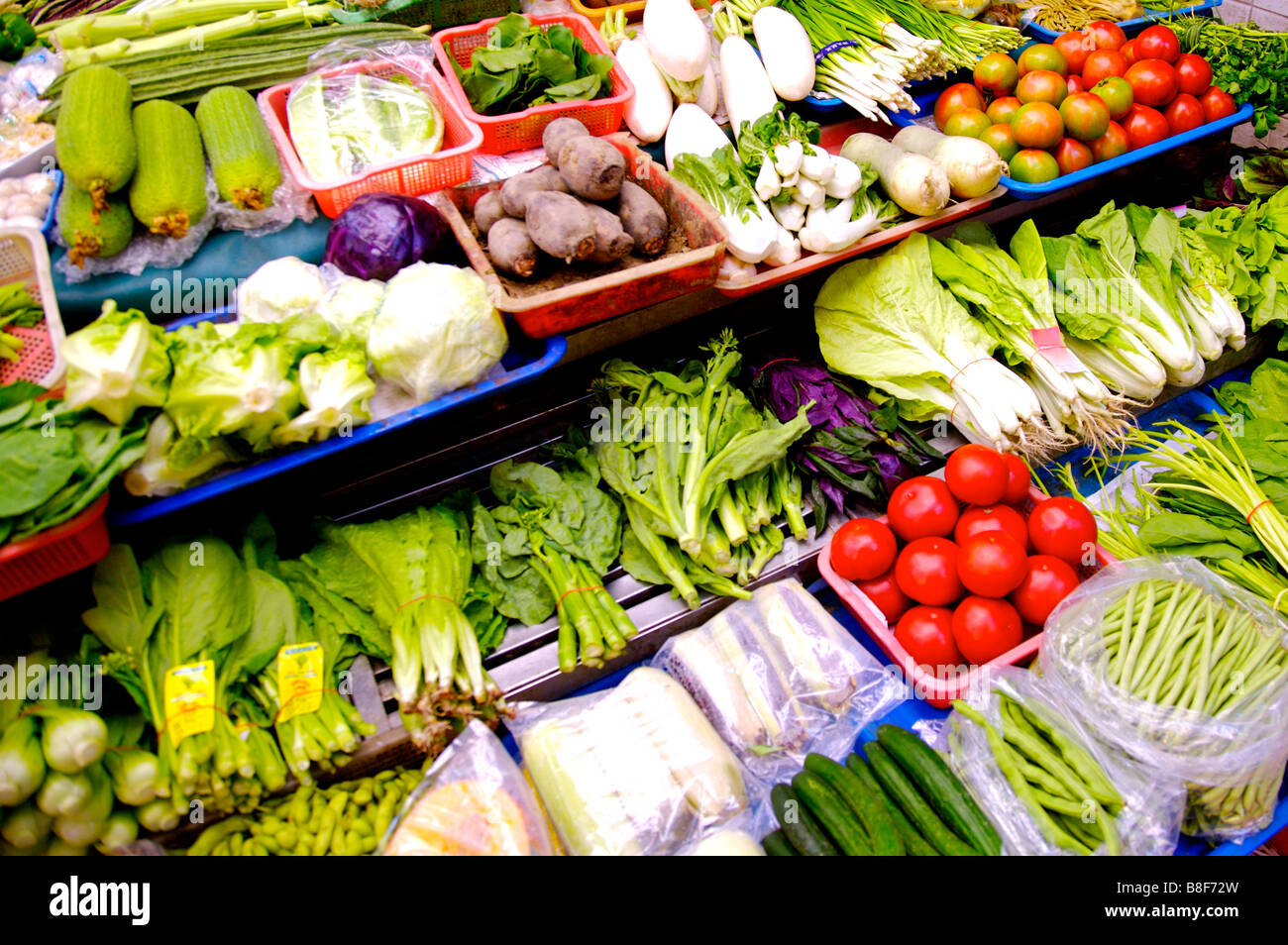 A variety of fresh vegetables on trays on display in a market stall ...