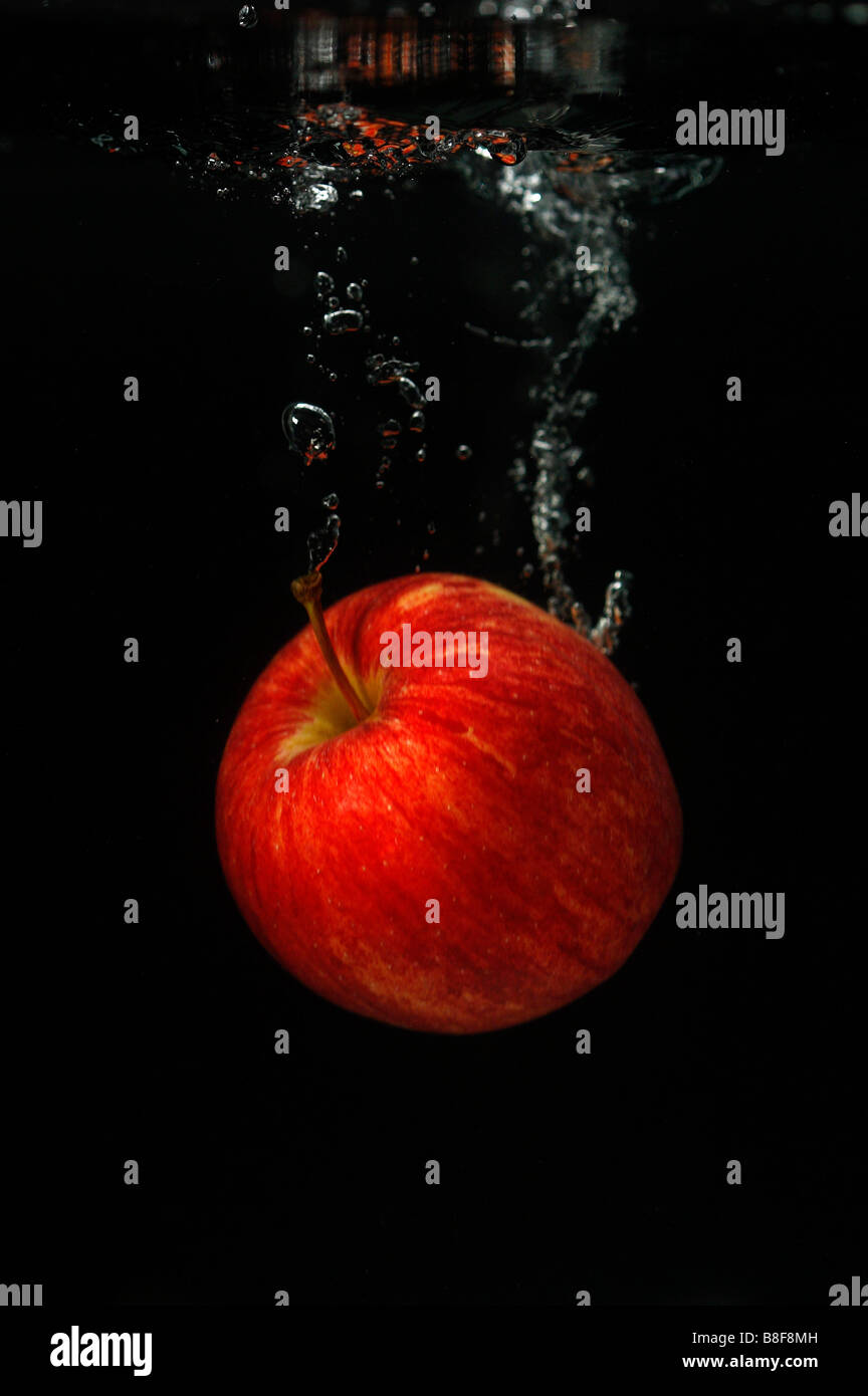 An apple falling into water against a black background creating water ...