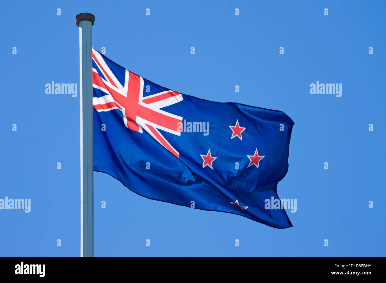 Backlit flying New Zealand flag on flagpost against blue sky Stock ...
