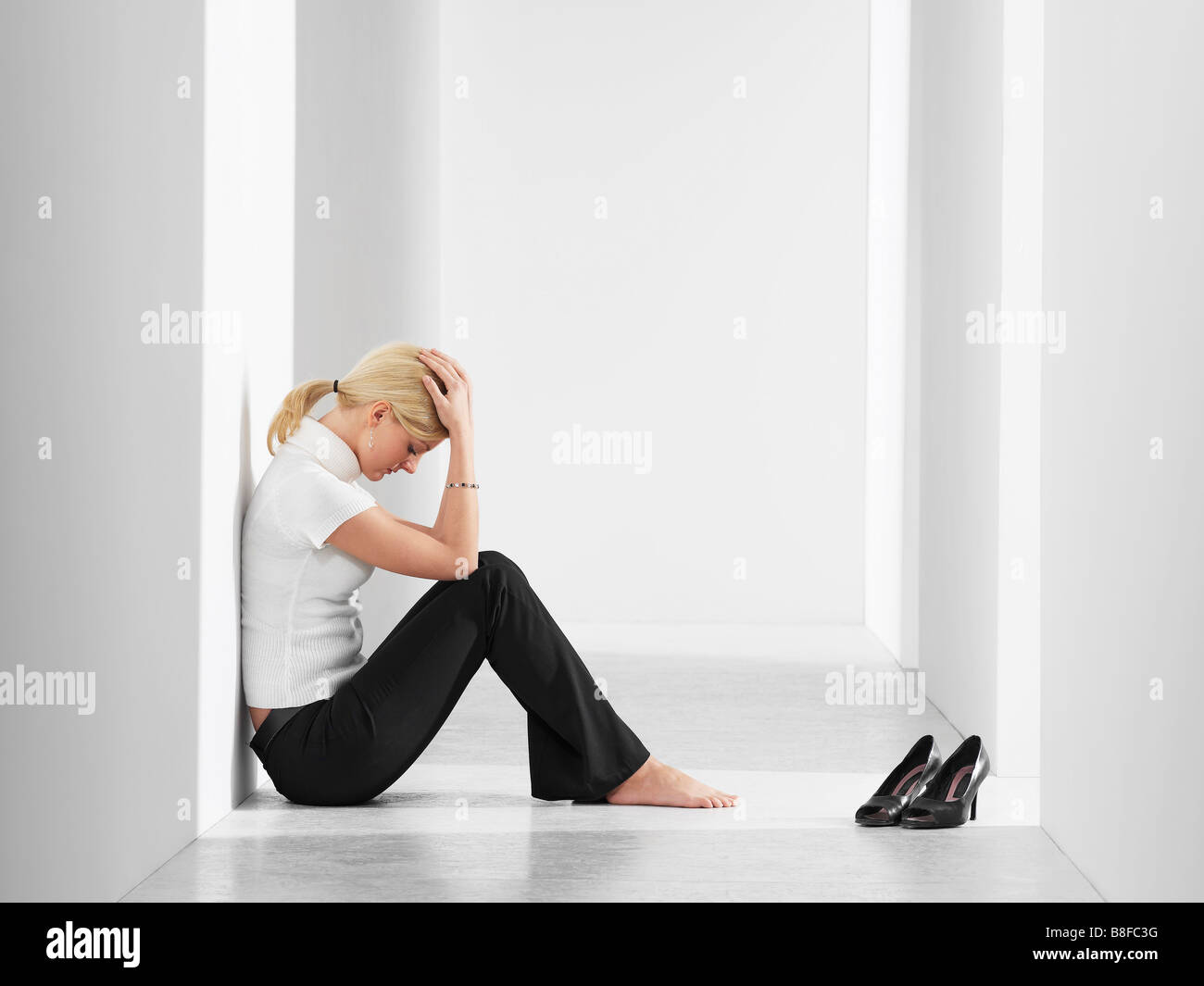 Frustrated woman sitting in a corridor Stock Photo - Alamy
