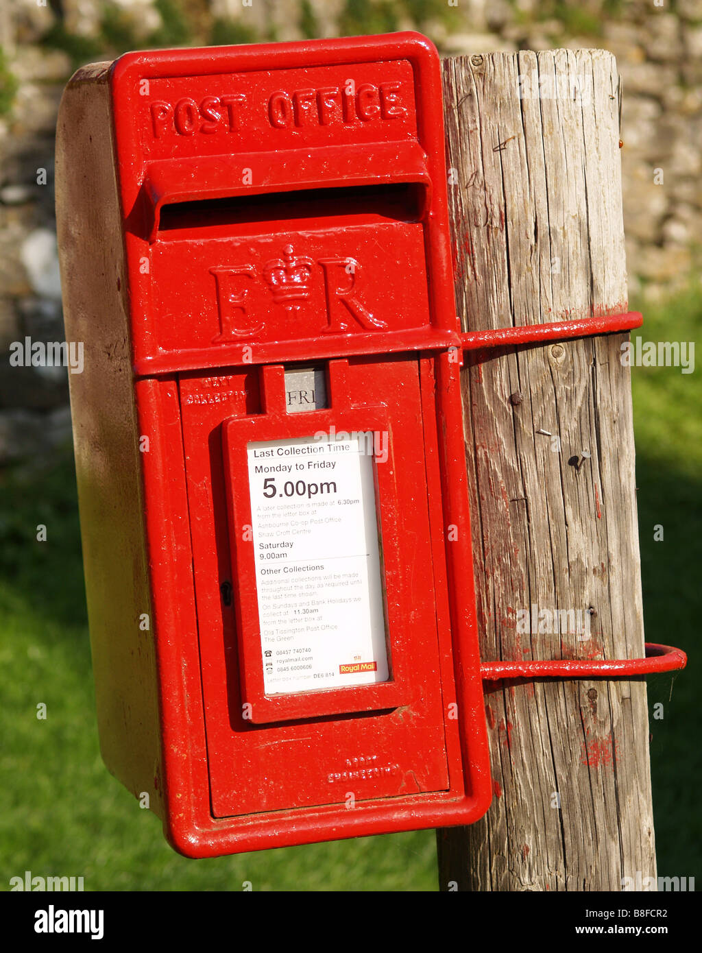 Close up of a square red village post box, attached to a wooden post ...