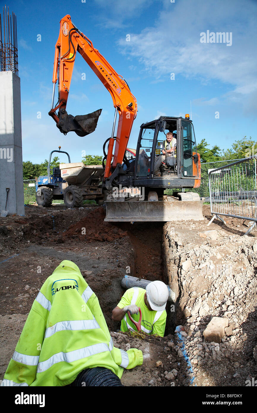 Jcb digging a trench on a construction site while a workman digs Stock ...