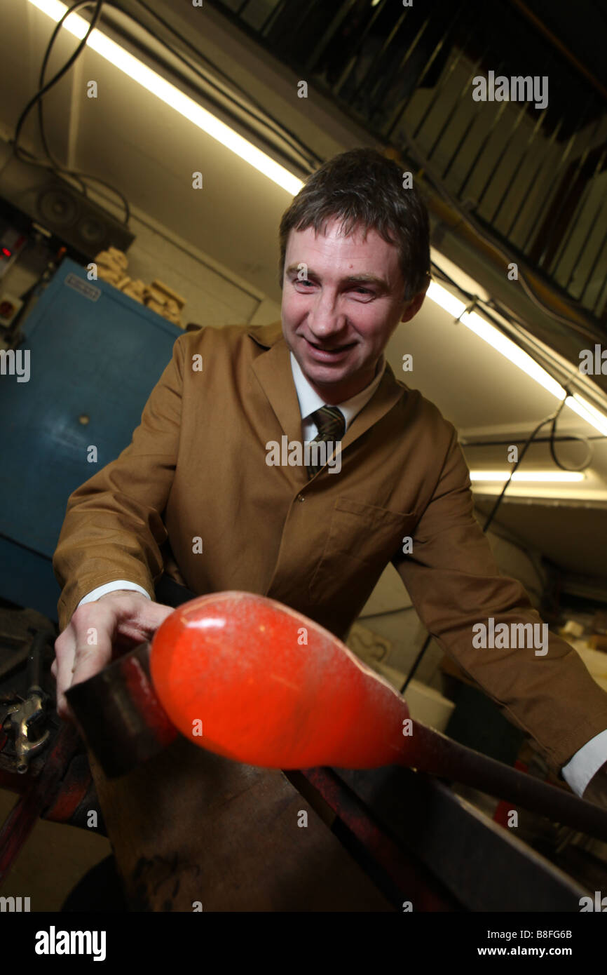 a professional glass blower takes some molten glass out of a furnace ...