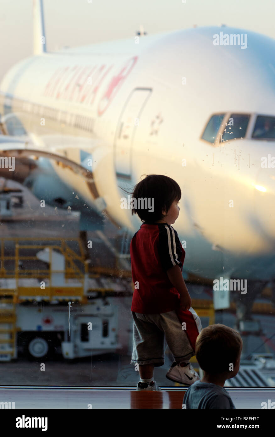 A young child looking out of an airport window with a plane behind ...