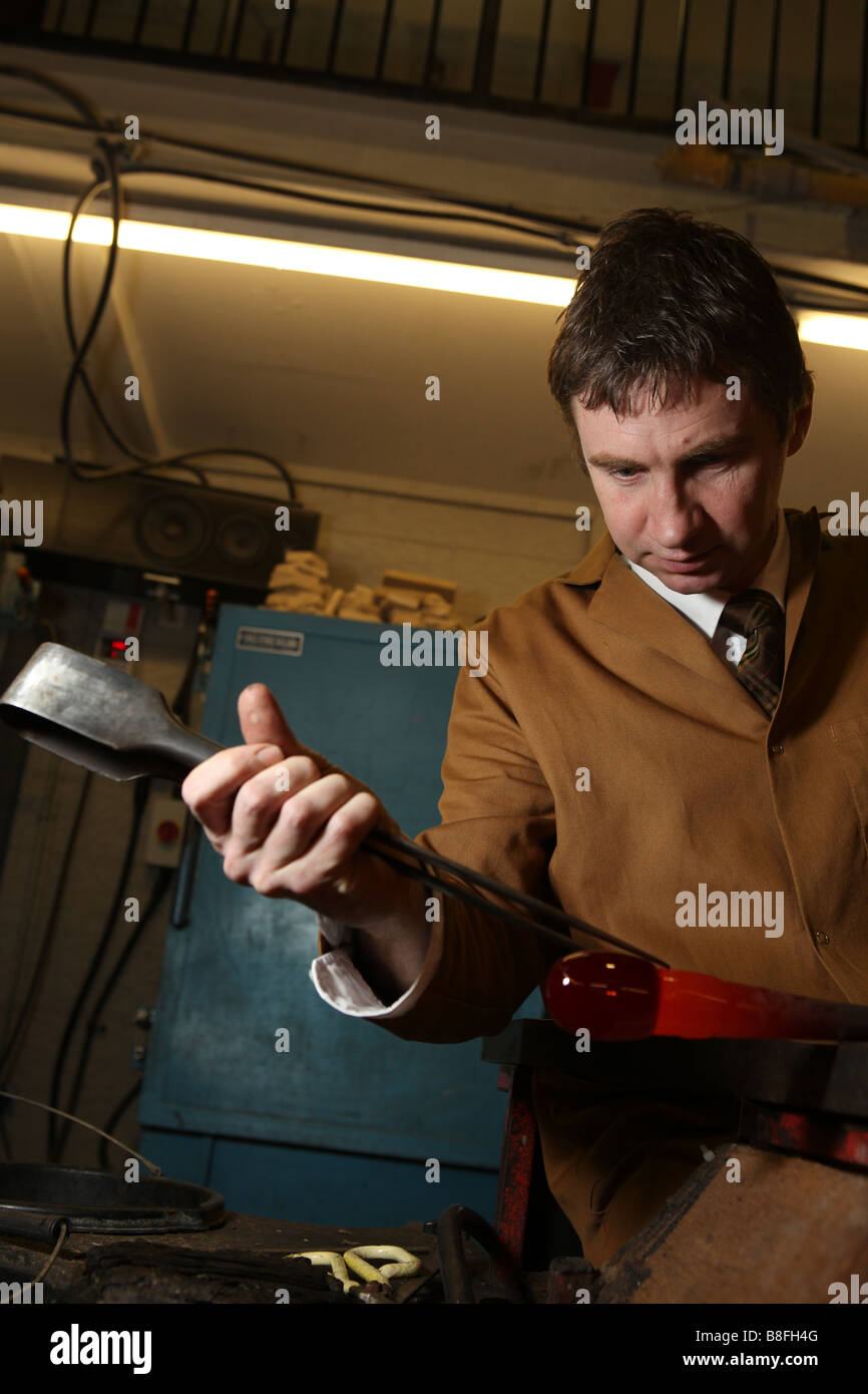 a professional glass blower takes some molten glass out of a furnace ...