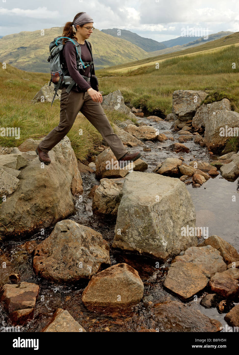 A young woman jumping across a river on stepping stones Stock Photo - Alamy