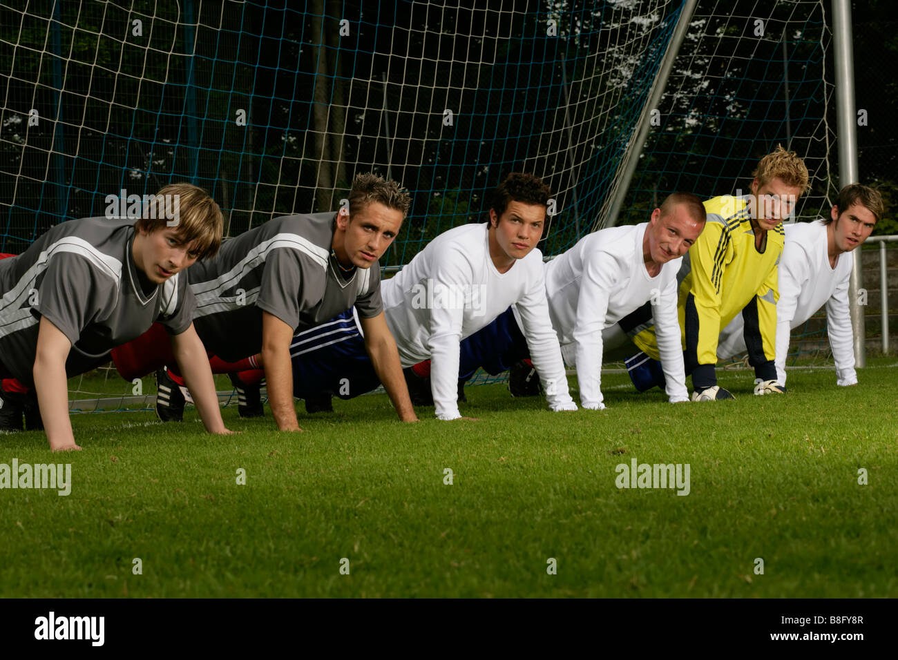 Six young footballers doing push-ups in front of a goal on a pitch ...
