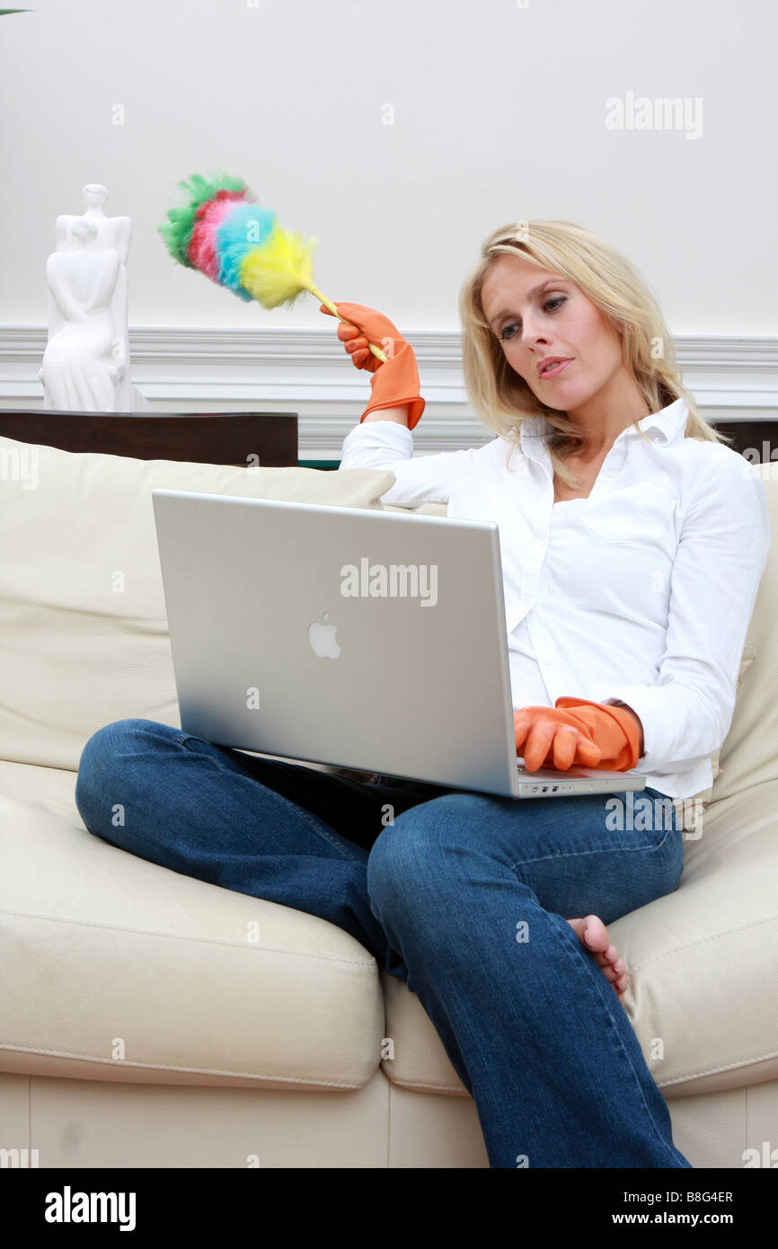 A thirty something woman sits on a sofa logging onto her computer ...